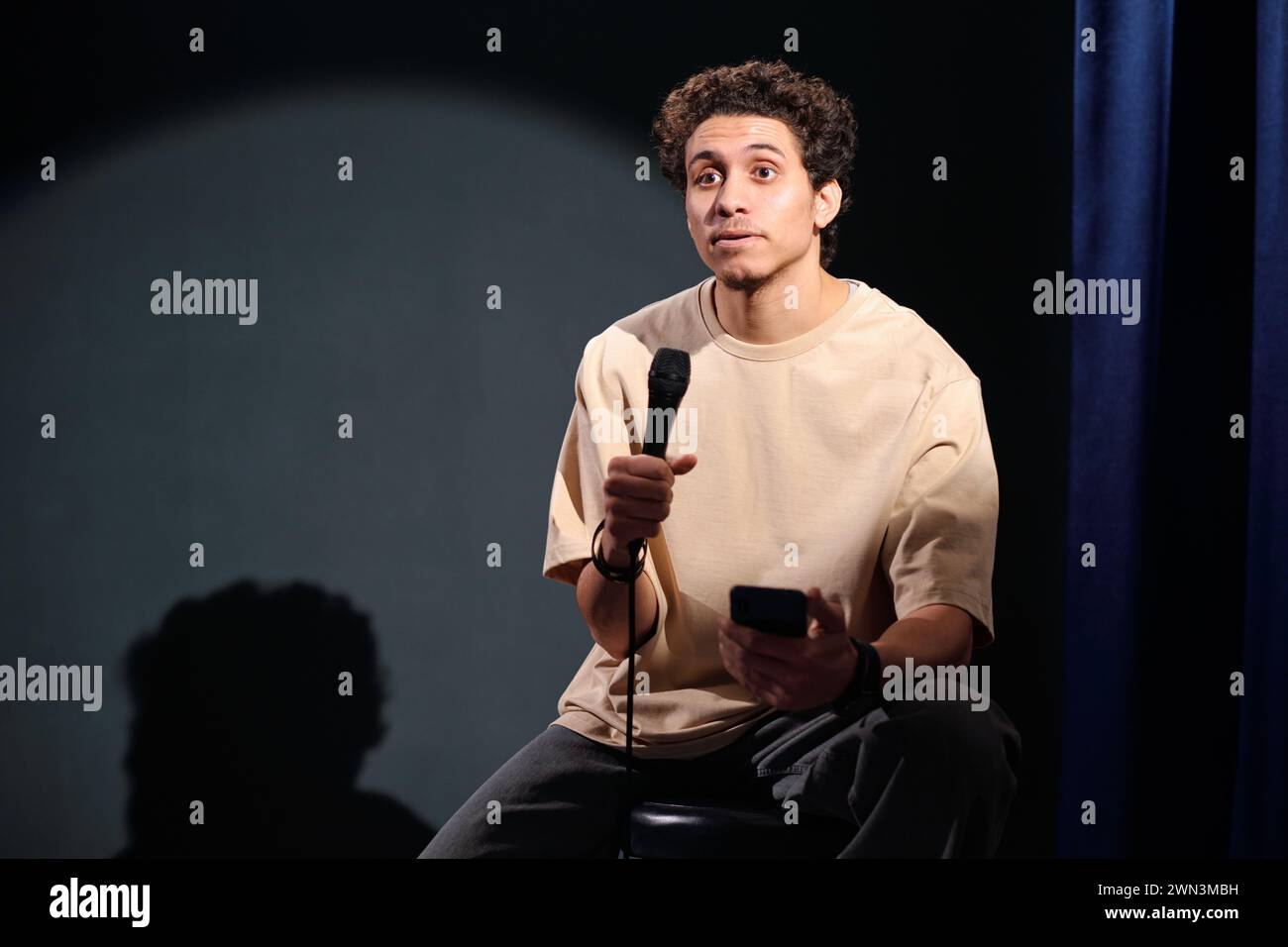 Comedian of stand up show speaking in microphone and using smartphone ...