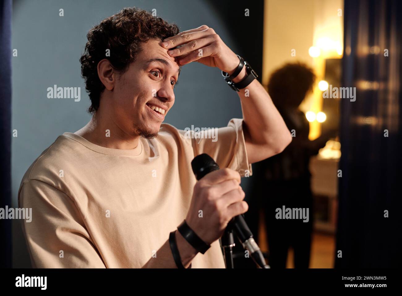 Young smiling male presenter with microphone standing on stage in front ...