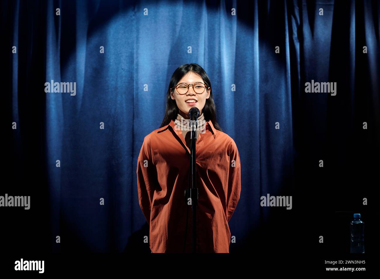 Young Chinese female comedian in brown shirt standing on stage with ...
