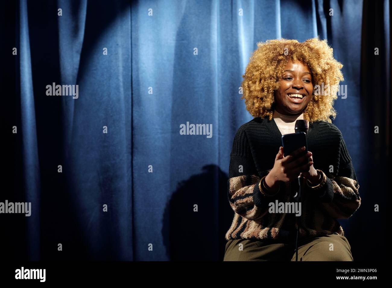 Young cheerful female stand up comedian scrolling in smartphone and ...