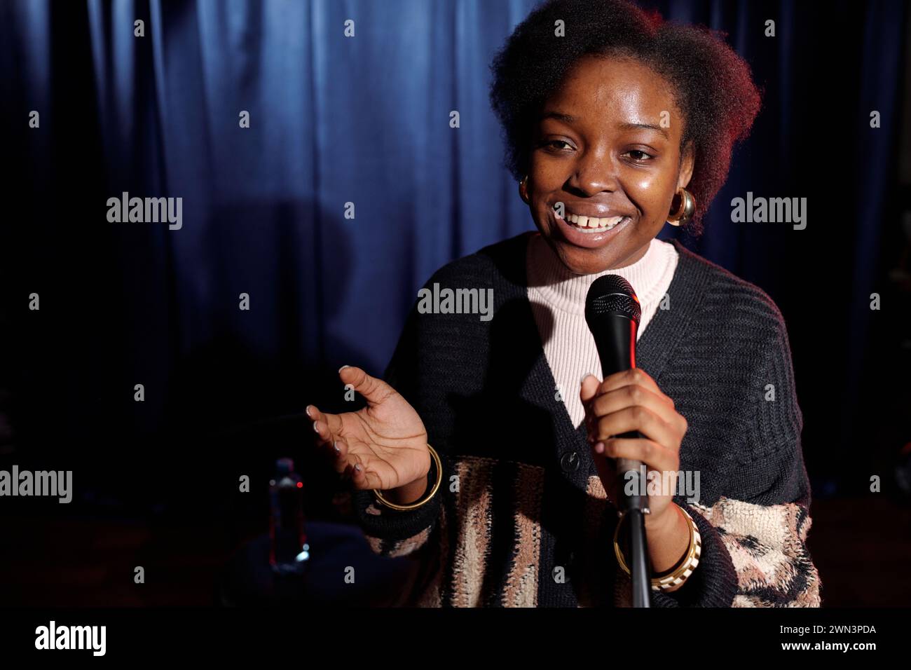 Happy young female comedian of modern stand up club holding microphone ...