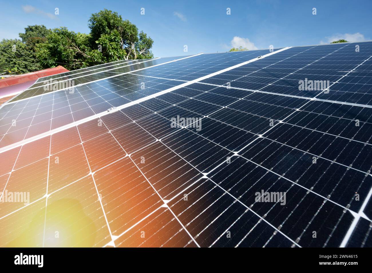 Solar panel array on house roof in blue sky and green tree background ...