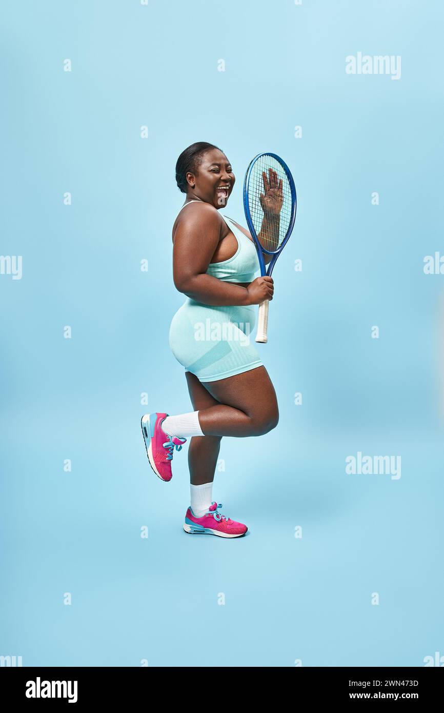 joyful plus size dark skinned woman holding tennis racket on blue ... joyful plus size dark skinned woman holding tennis racket on blue ...