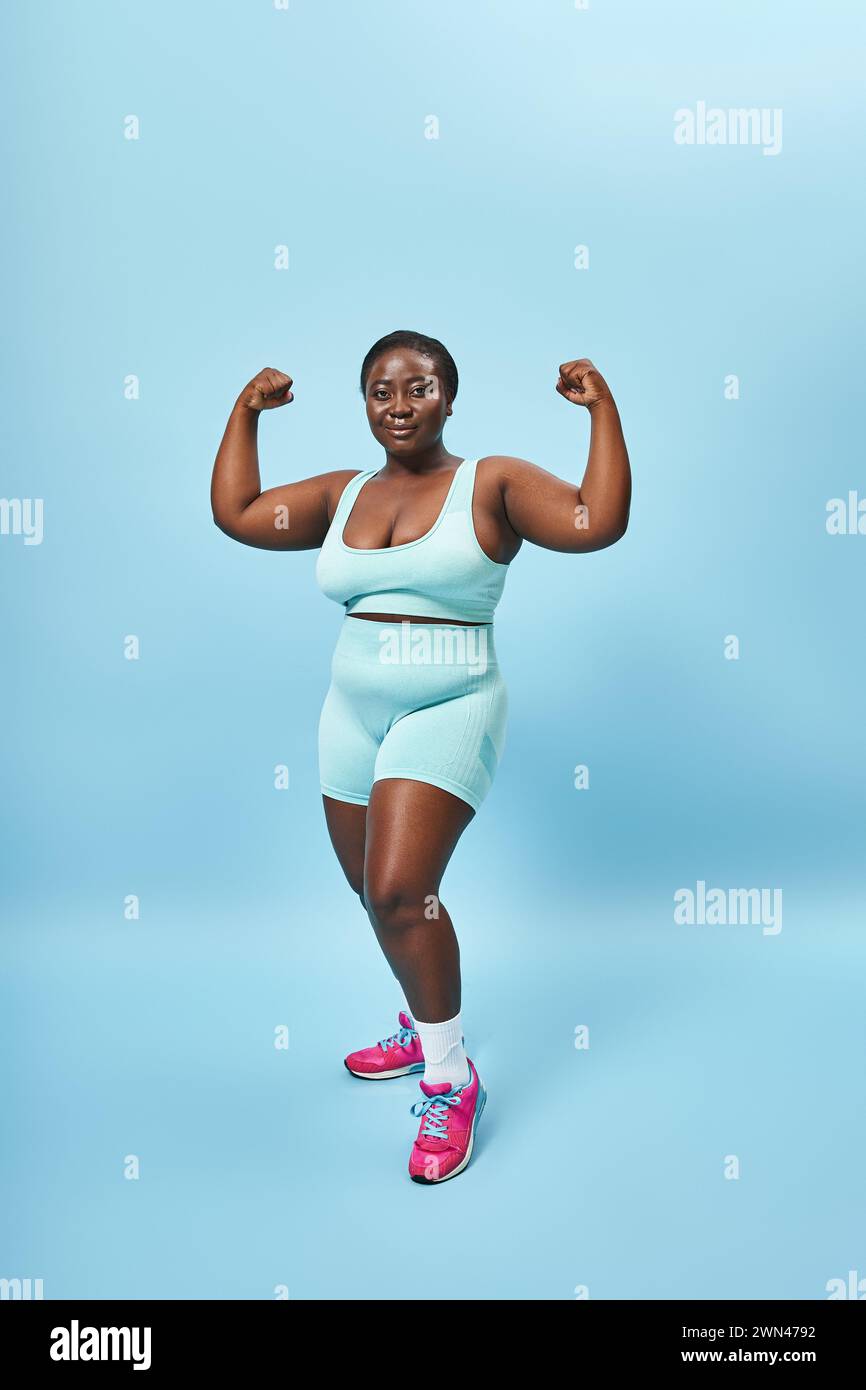 strong plus size woman in active wear flexing her muscles and looking ...