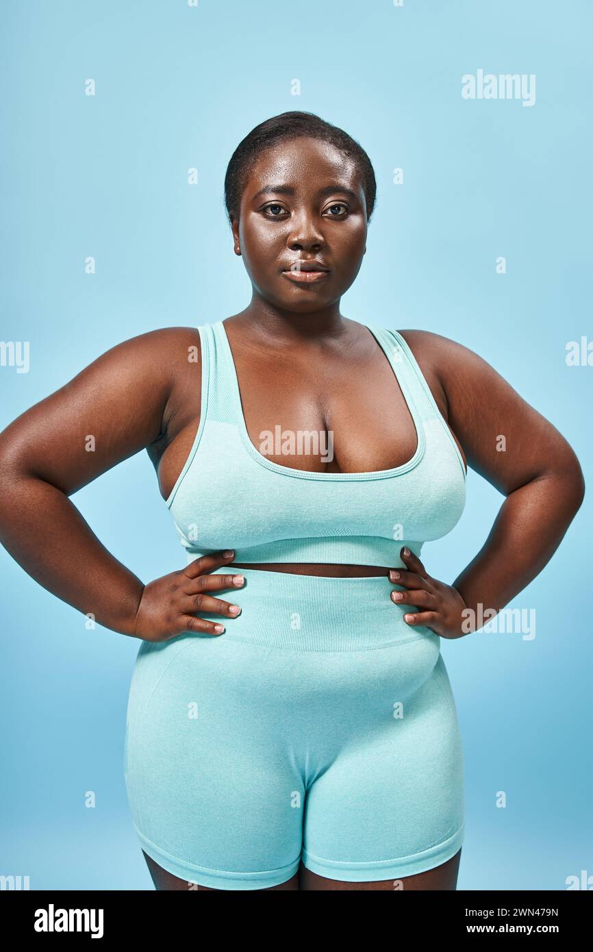 strong plus size african american woman in blue sportswear with hands on hips on matching ...