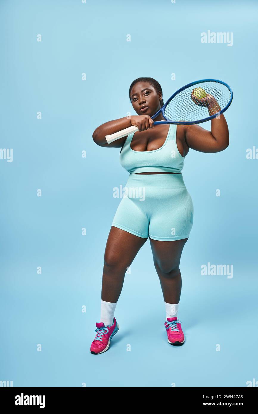 confident plus size african american woman ready to play tennis on blue ...