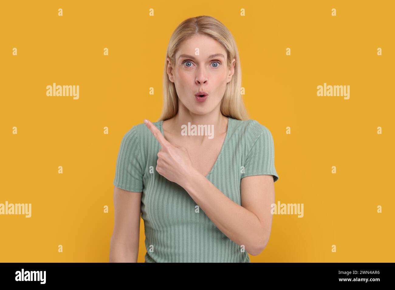 Surprised woman pointing at something on yellow background Stock Photo ...