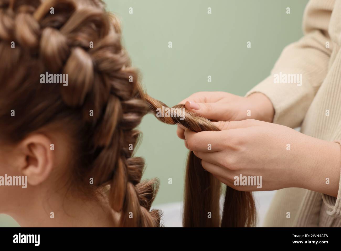 Professional stylist braiding woman's hair on olive background, closeup ...