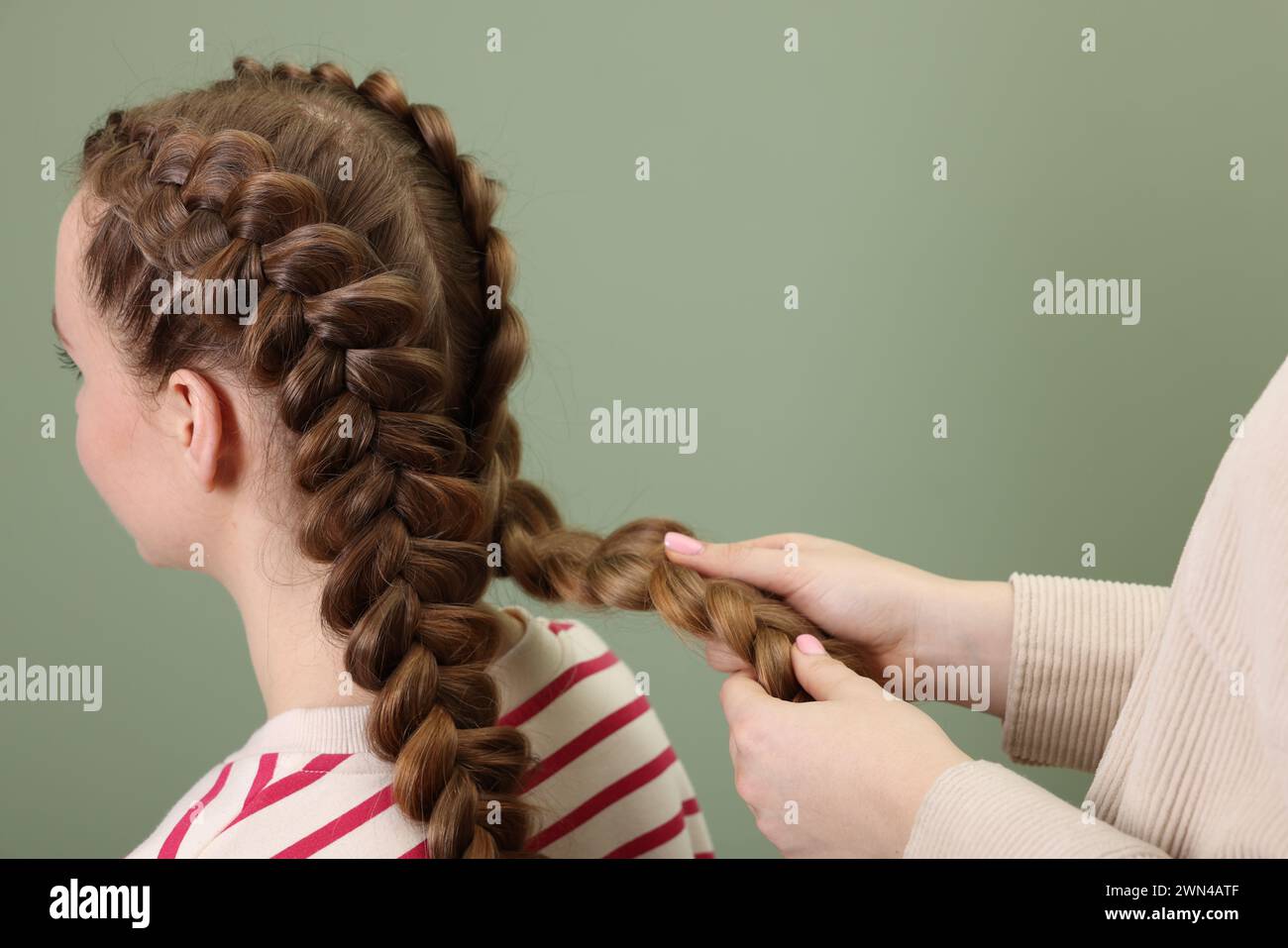 Professional stylist braiding woman's hair on olive background, closeup ...