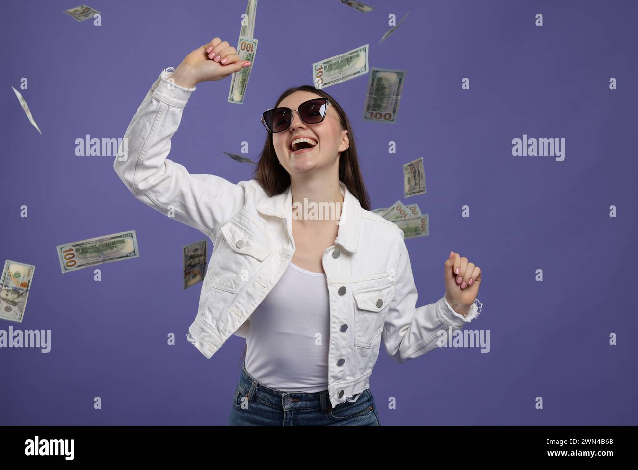 Happy woman under money shower on purple background Stock Photo - Alamy