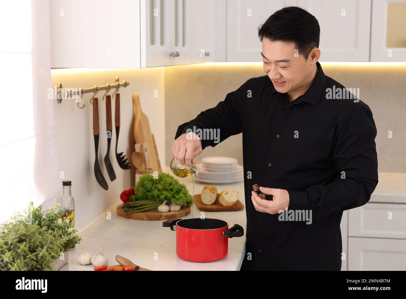 Cooking process. Man pouring oil into pot at countertop in kitchen ...