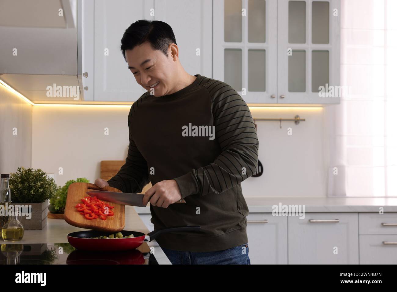 Cooking process. Man adding cut bell pepper into frying pan in kitchen ...