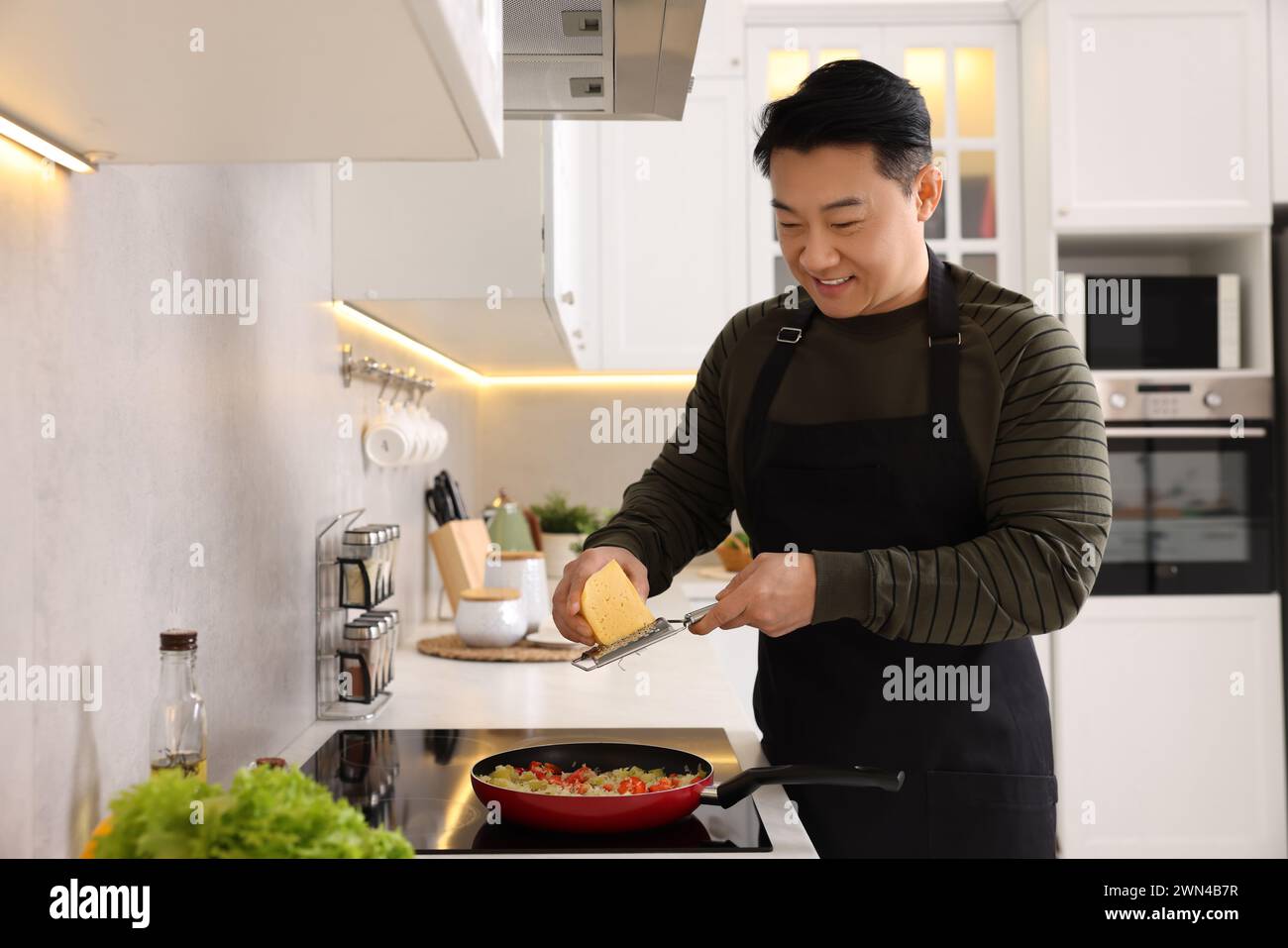 Cooking process. Man grating cheese into frying pan in kitchen Stock ...