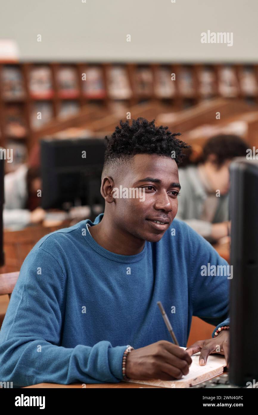 Vertical portrait of smiling young Black man looking at computer screen ...