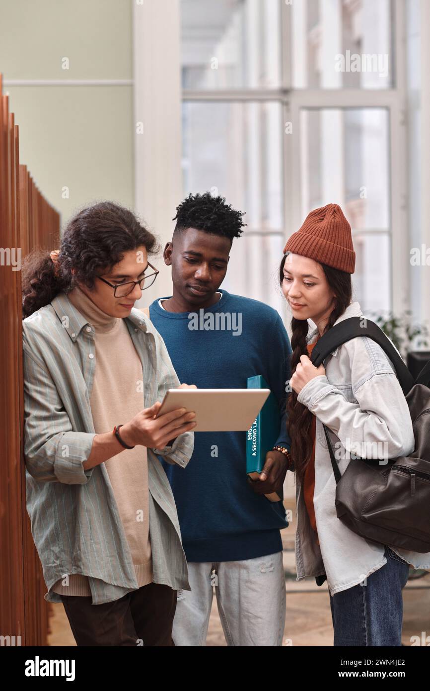 Vertical portrait of diverse group of three young students looking at ...