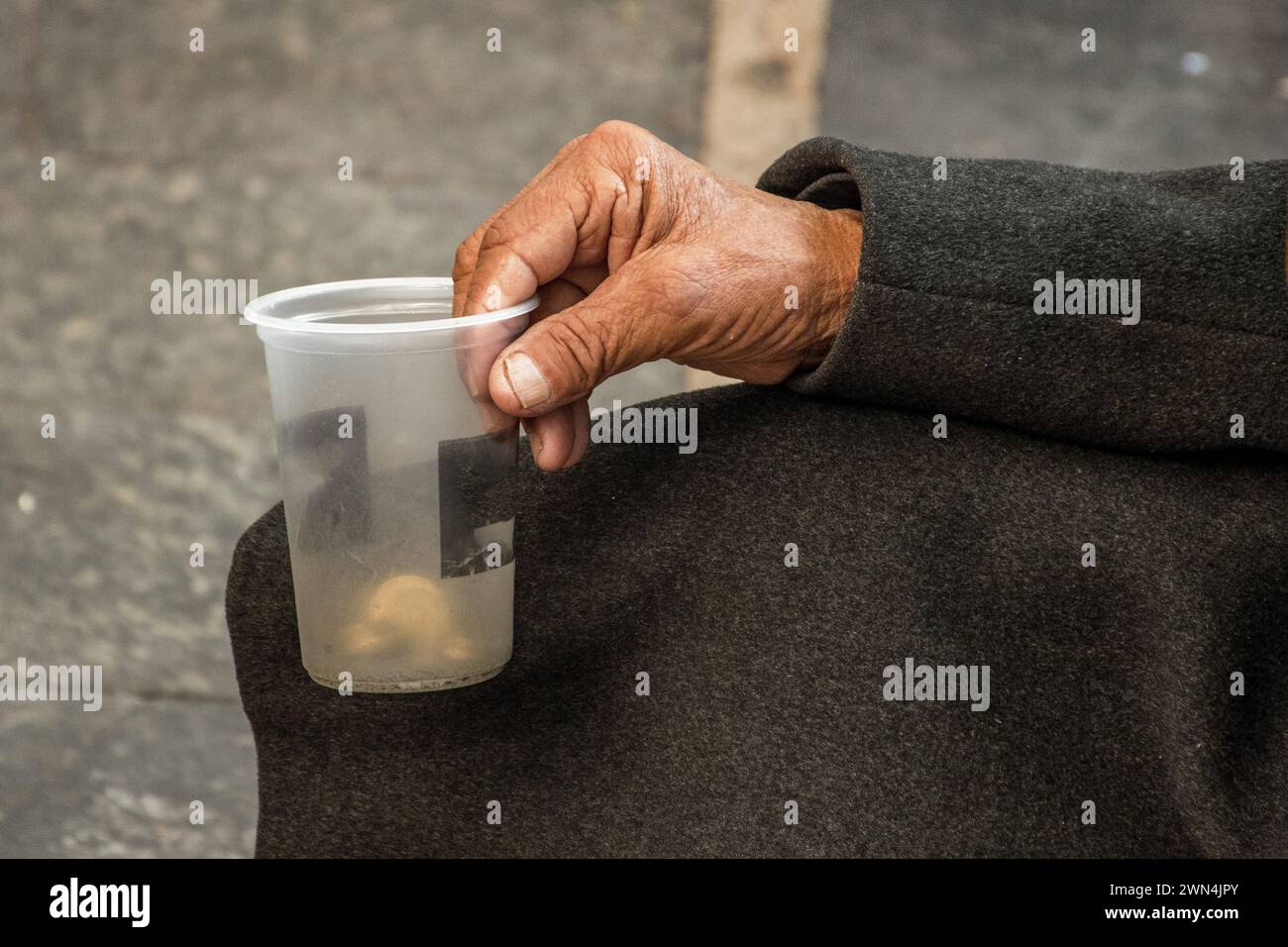 Closeup of a man's hand clasping a clear plastic cup and begging for ...