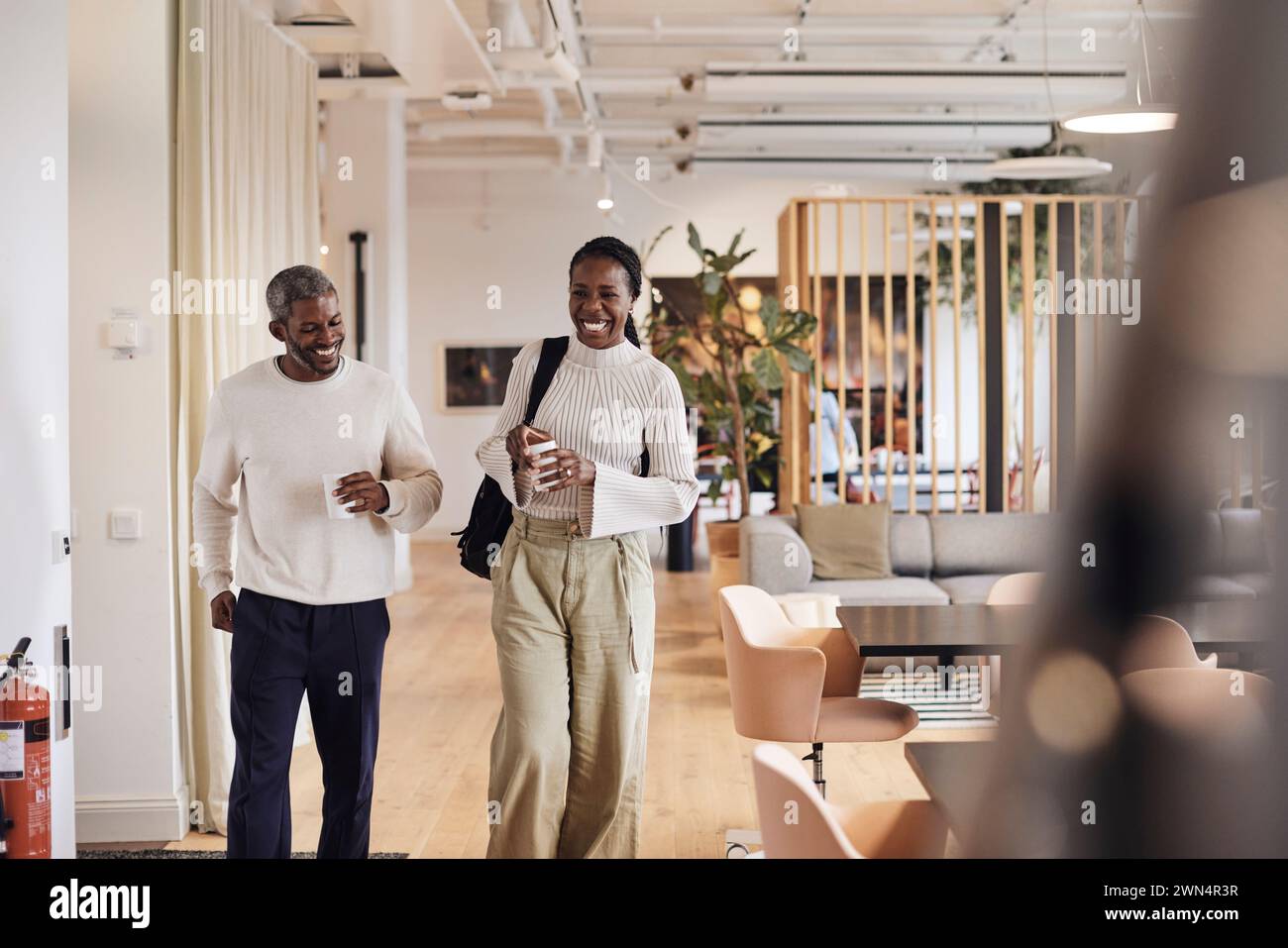 Happy male and female business professionals walking in office corridor ...