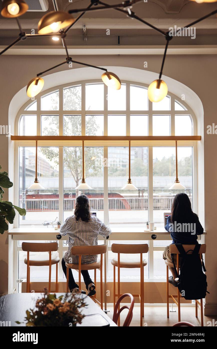 Rear view of businesswomen working on laptop while sitting on chair ...