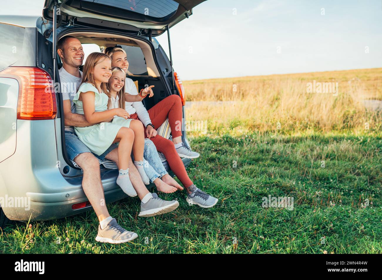 Portrait of Happy young couple with little daughters sitting inside car trunk during auto trop ...