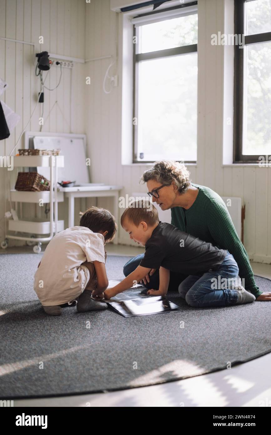 Schoolboys studying with senior female teacher while sitting on ...