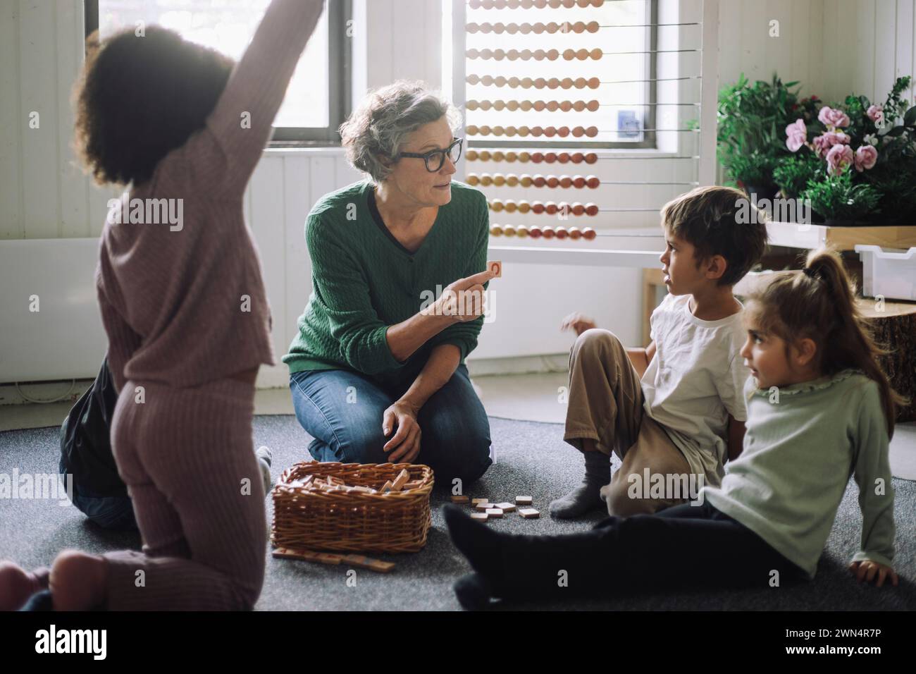 Senior female teacher playing puzzle game with preschool children while ...