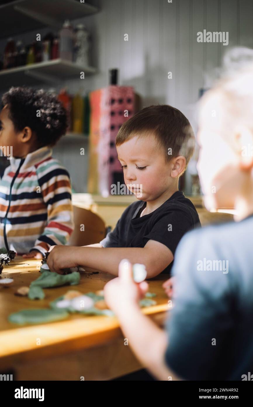 Schoolboy playing with clay while sitting at bench during art class at ...