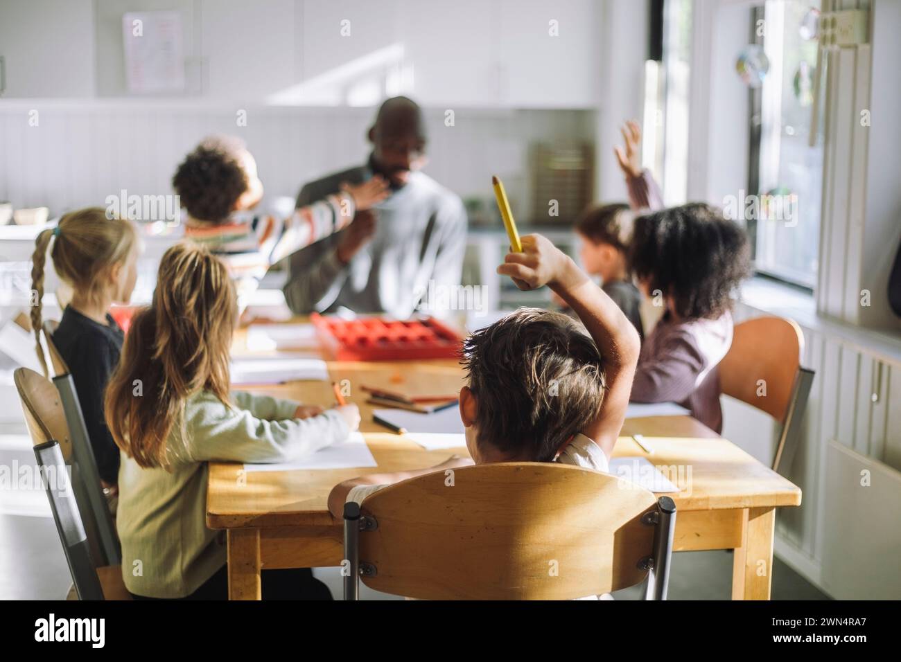 Boy raising hand while sitting in classroom during Q and A session at ...