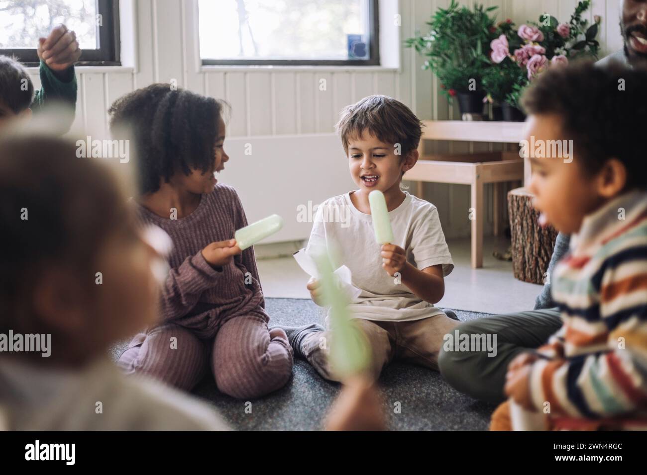 Boy and girl holding popsicle stick while sitting in classroom at ...