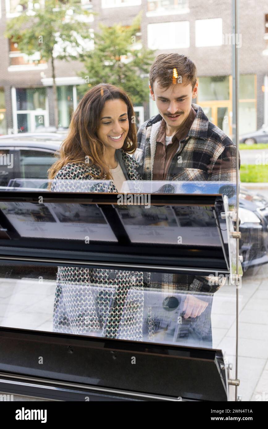Smiling young couple looking at placard on glass window of real estate ...