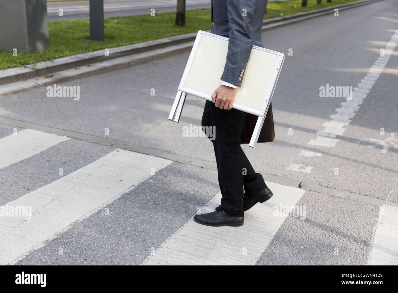 Low section of real estate agent carrying placard while crossing street ...