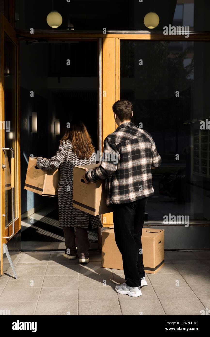 Multiracial couple carrying boxes while walking in apartment building ...