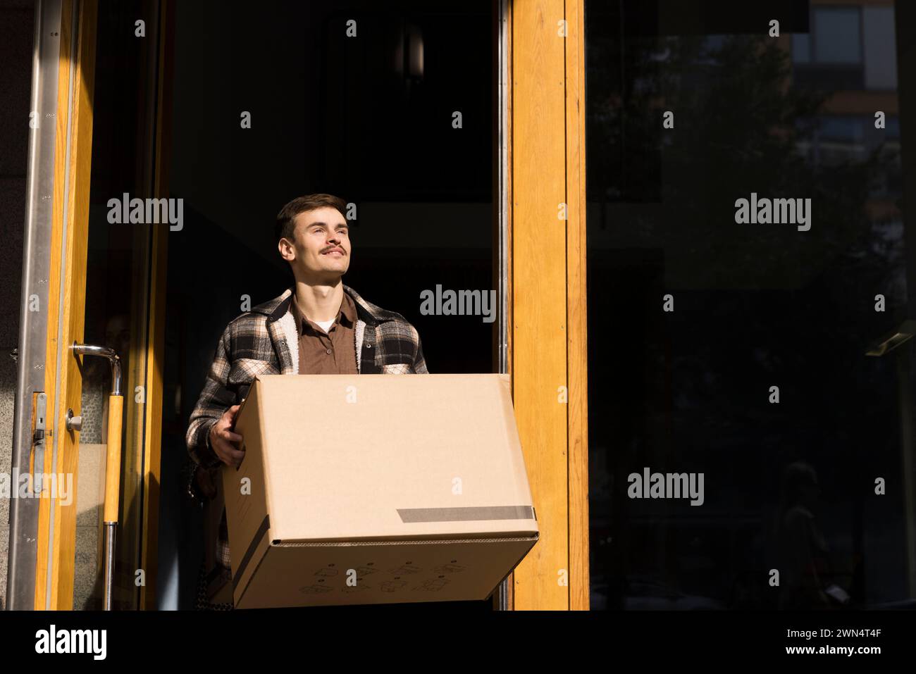 Contemplative man carrying box while leaving from apartment building ...