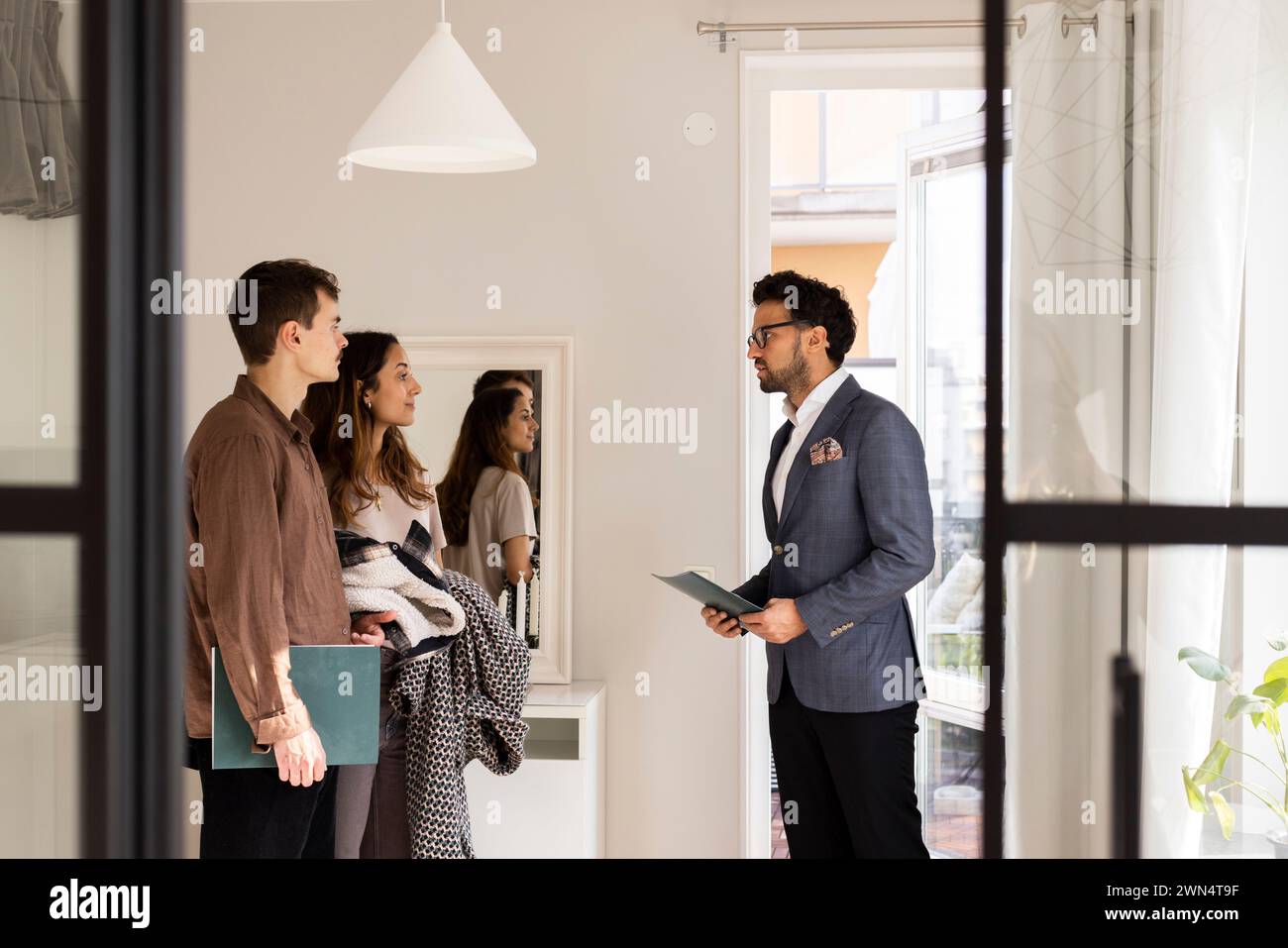 Salesman discussing with male and female clients while standing at home ...