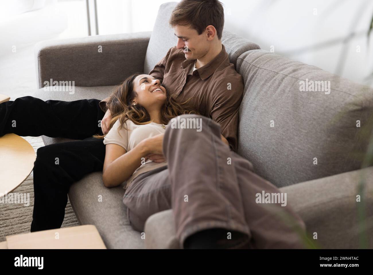 Smiling woman lying down on boyfriend's lap sitting on sofa at home ...