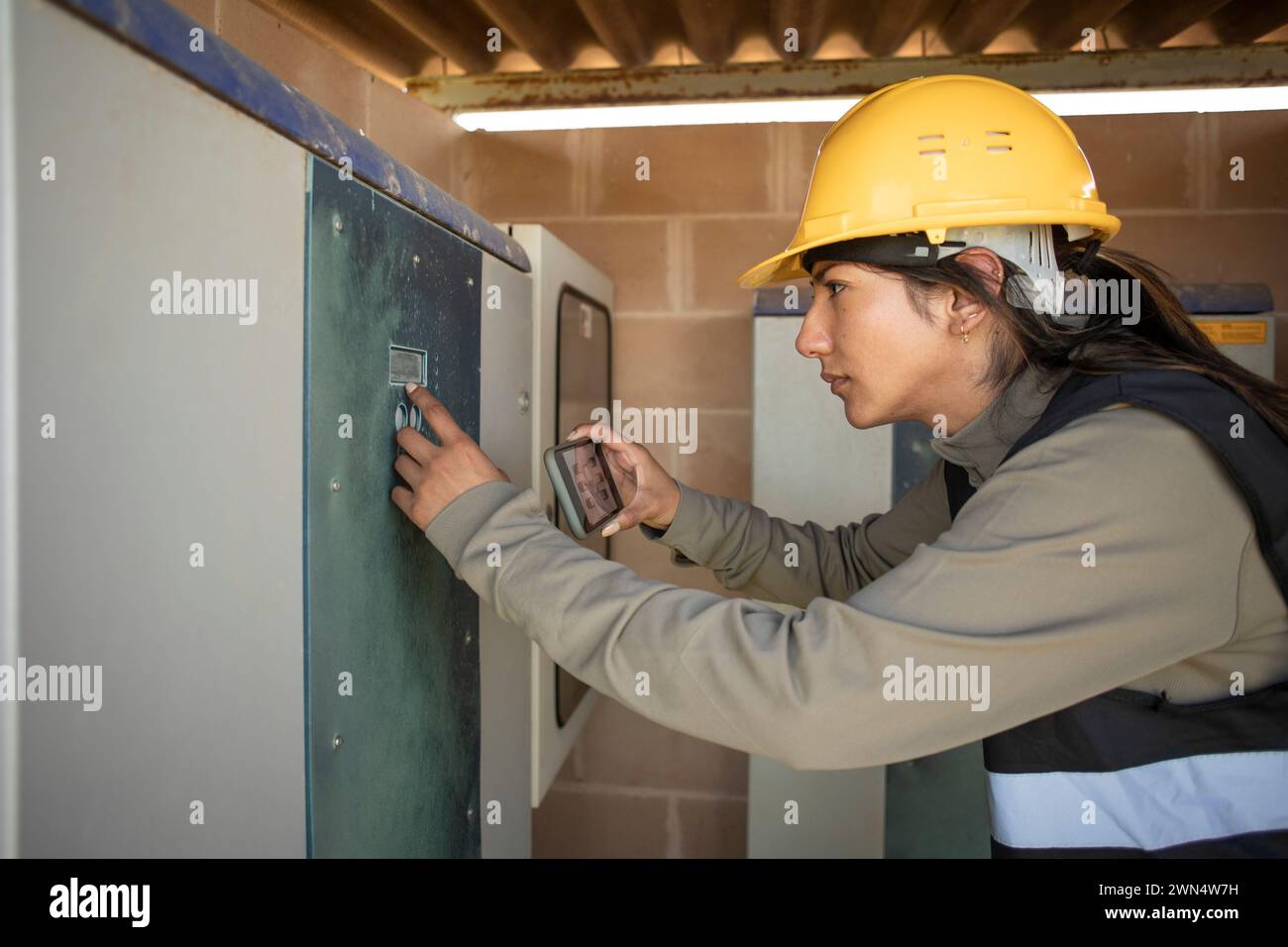 Side view of female engineer programming fuse box through smart phone ...