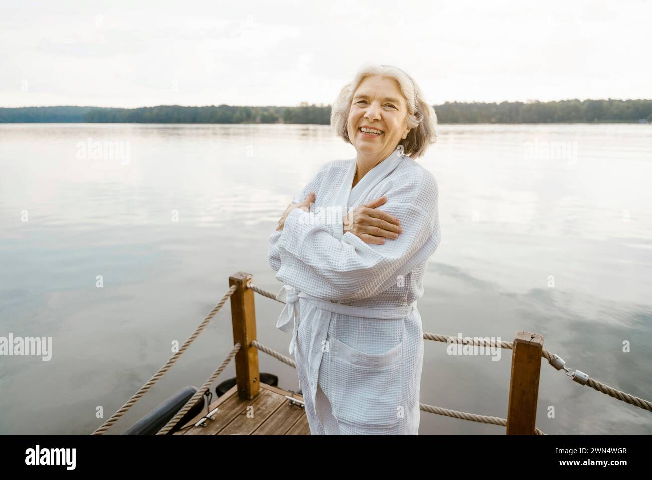 Portrait Of Happy Senior Woman Wearing White Bathrobe Hugging Self On