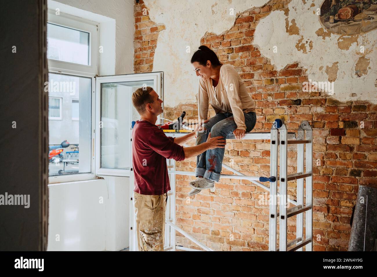 Man talking with woman sitting on ladder in front of brick wall during ...