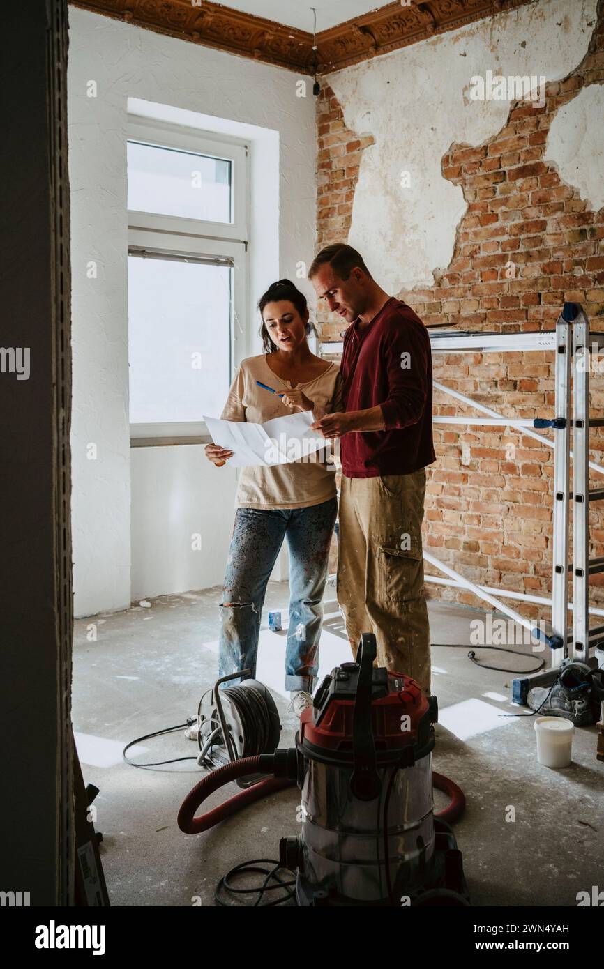 Couple discussing over blueprint in room while renovating home Stock ...