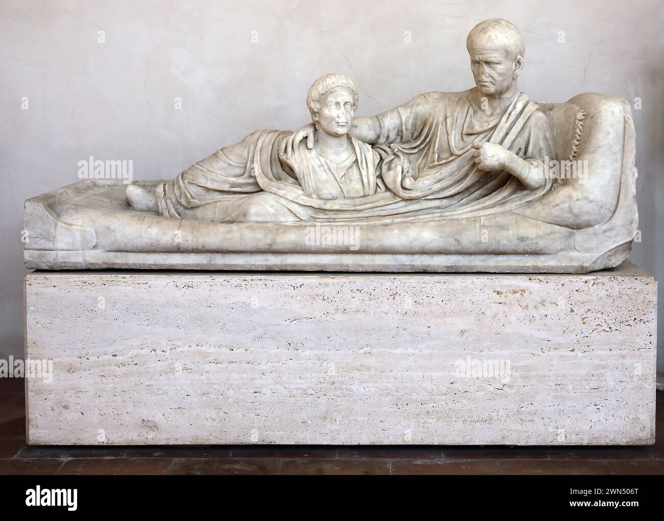 Kline funerary monument, on which the deceased is lying wearing a toga and holding a bust of a ...