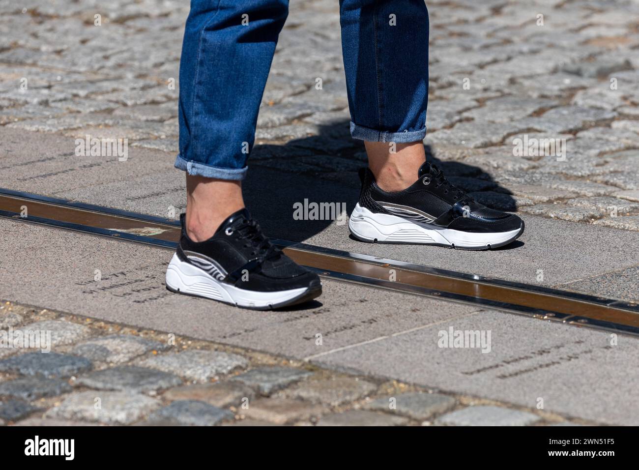 Pair of feet with black sneakers standing on both sides of meridian ...