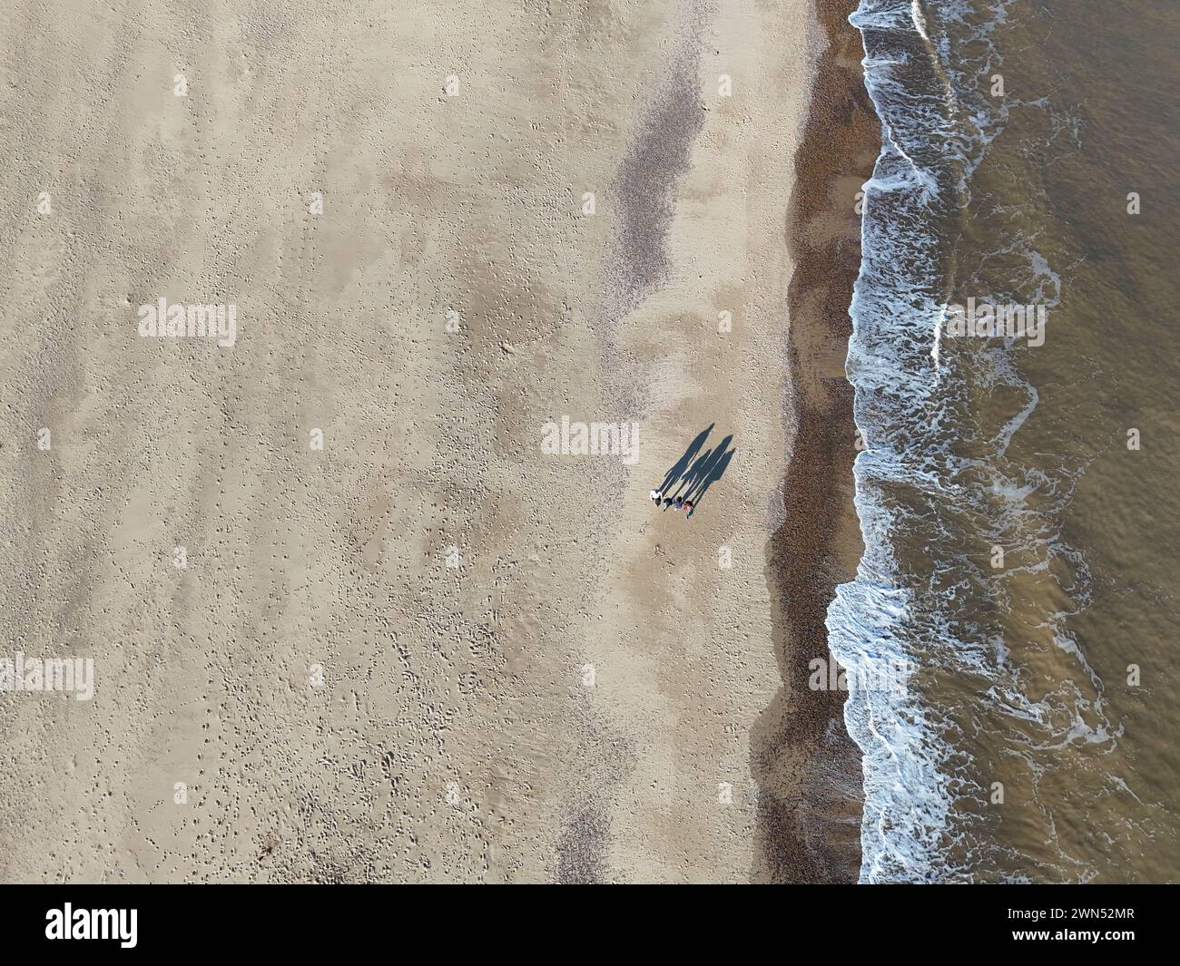 Overhead birds eye drone aerial view people walking on beach long ...