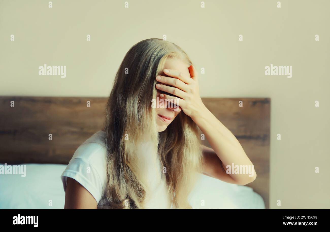 Upset sad crying woman covering her eyes with hands on the bed ...
