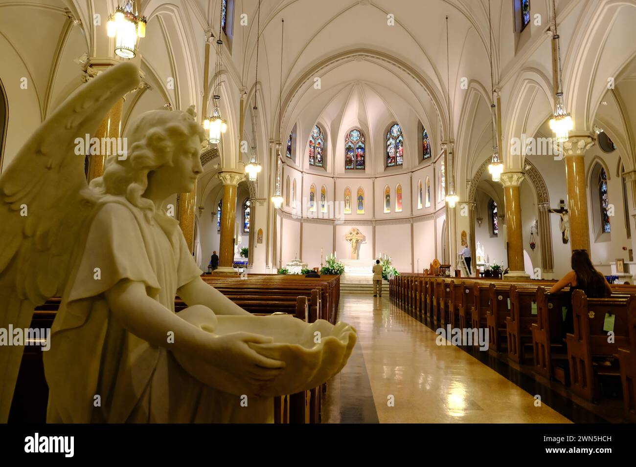 An angel statue holding a holy water stoup with nave and the main altar ...
