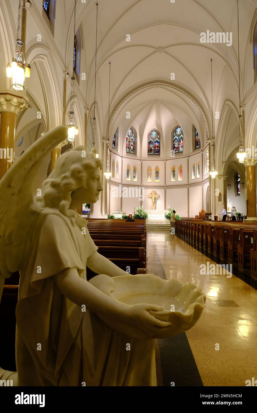 An angel statue holding a holy water stoup with nave and the main altar ...