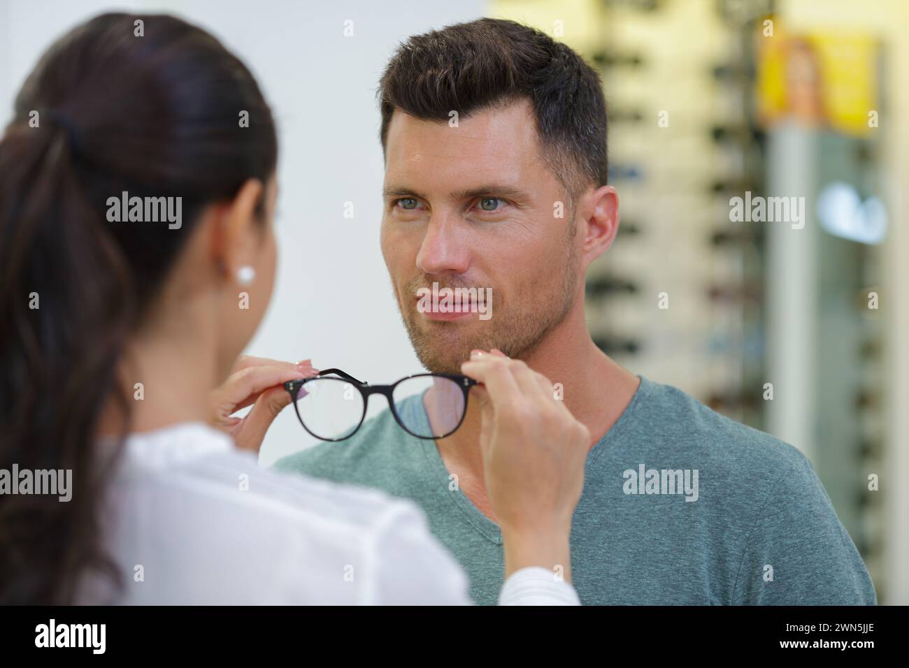 female optician fitting glasses onto male customer Stock Photo - Alamy