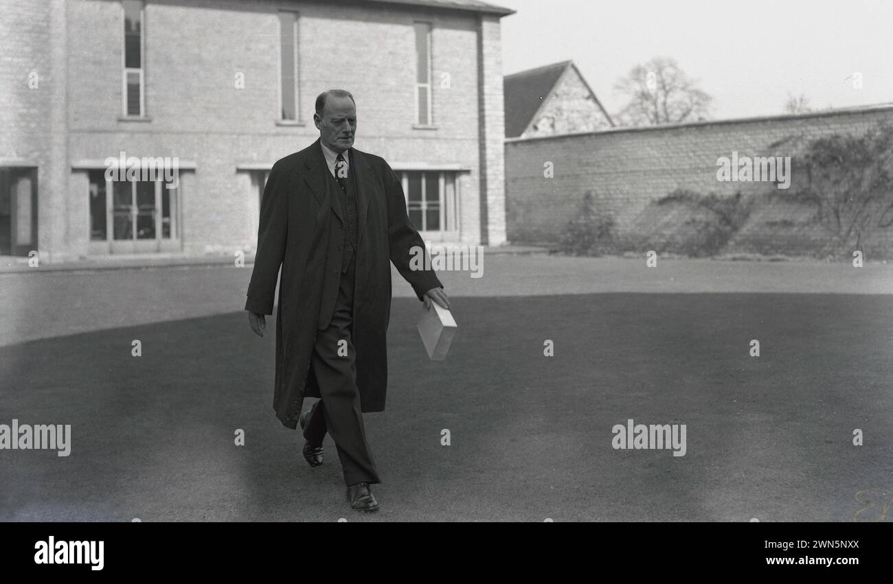 Late 1950s, historical, college warden or dean in coat walking outside ...