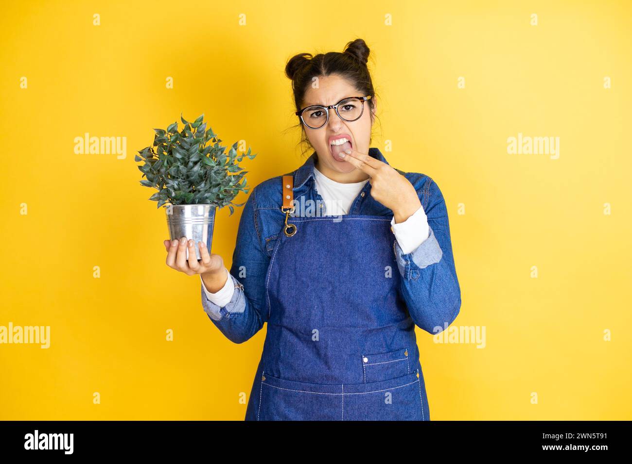 Young caucasian gardener woman holding a plant isolated on yellow ...
