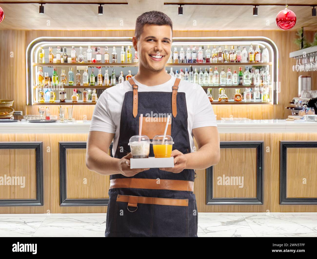 Male waiter holding takeaway coffee and fresh orange juice at a bar ...