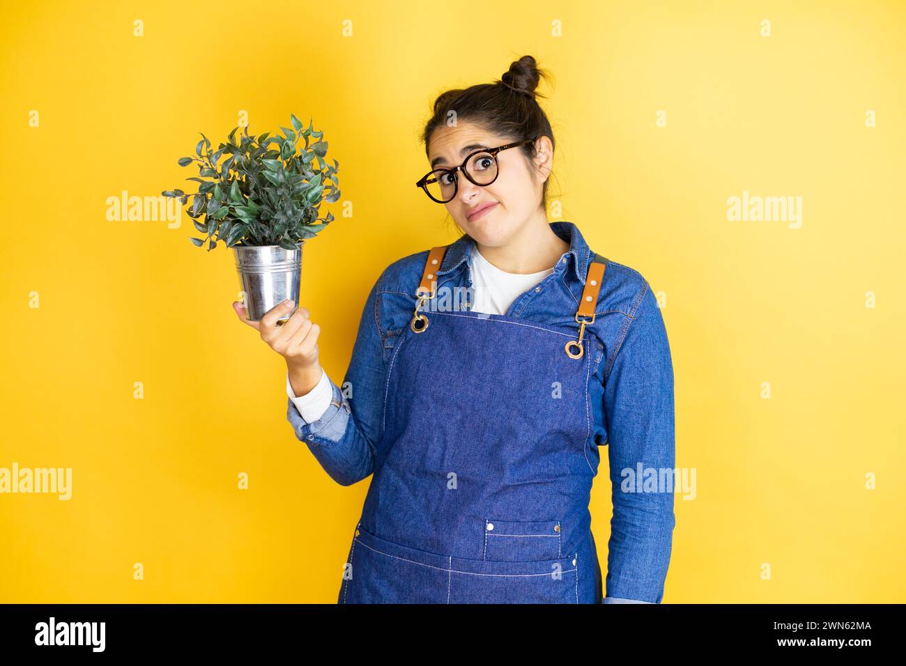 Young caucasian gardener woman holding a plant isolated on yellow ...