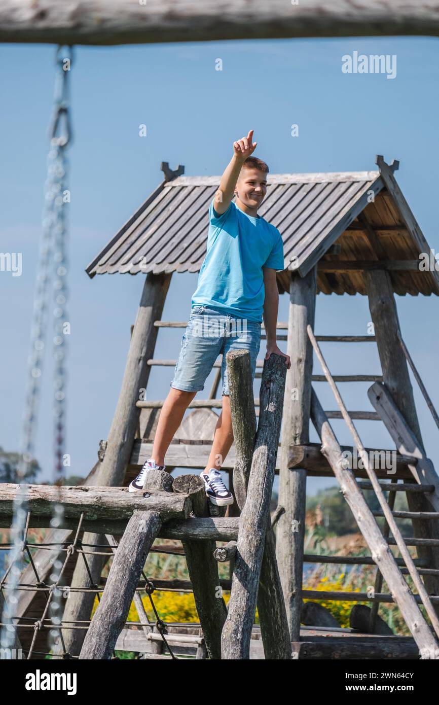 A boy in a blue shirt waves atop a rustic wooden structure, playground ...